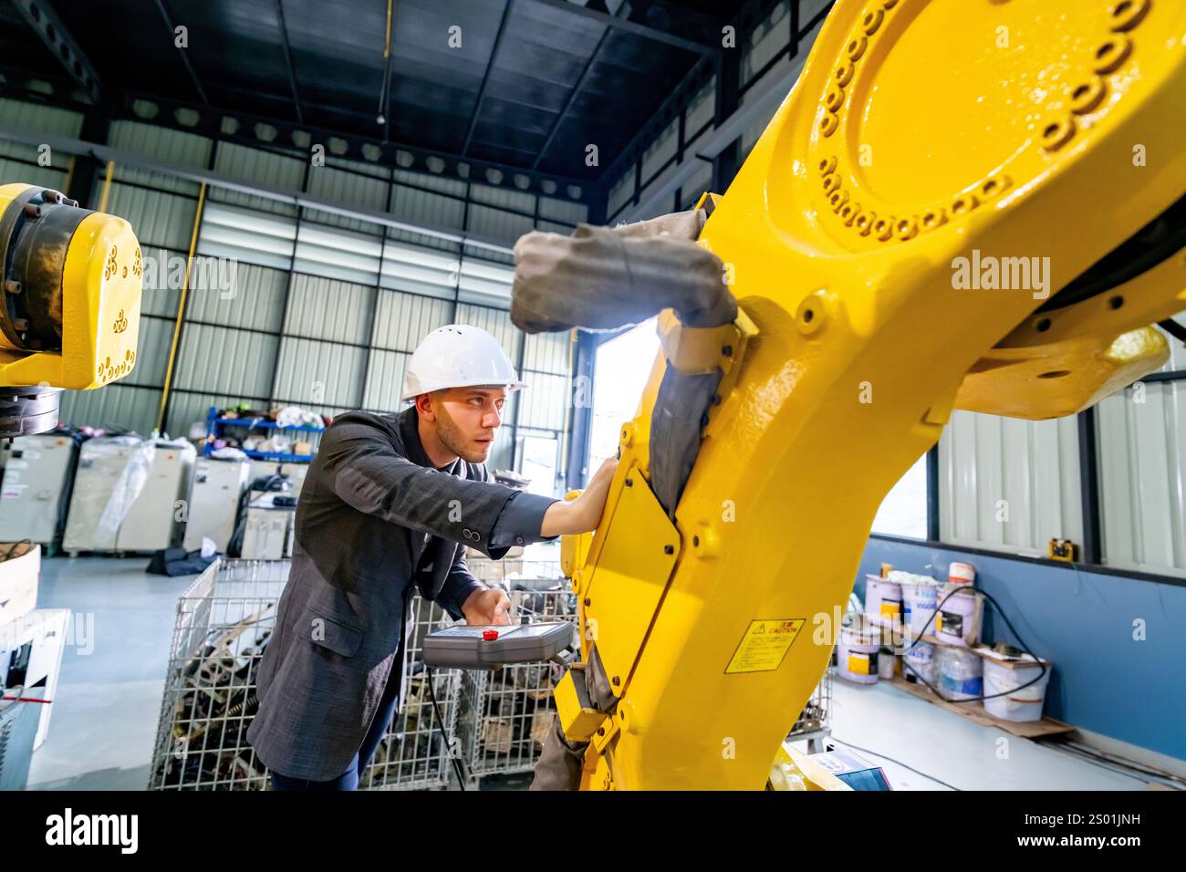 A professional in a hard hat examines a yellow robotic arm, ensuring ...