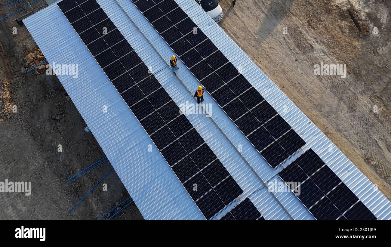 Workers are installing solar panels on a metal rooftop at a ...
