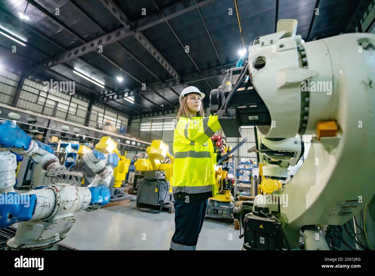 A worker in a reflective safety jacket and hardhat stands in a ...