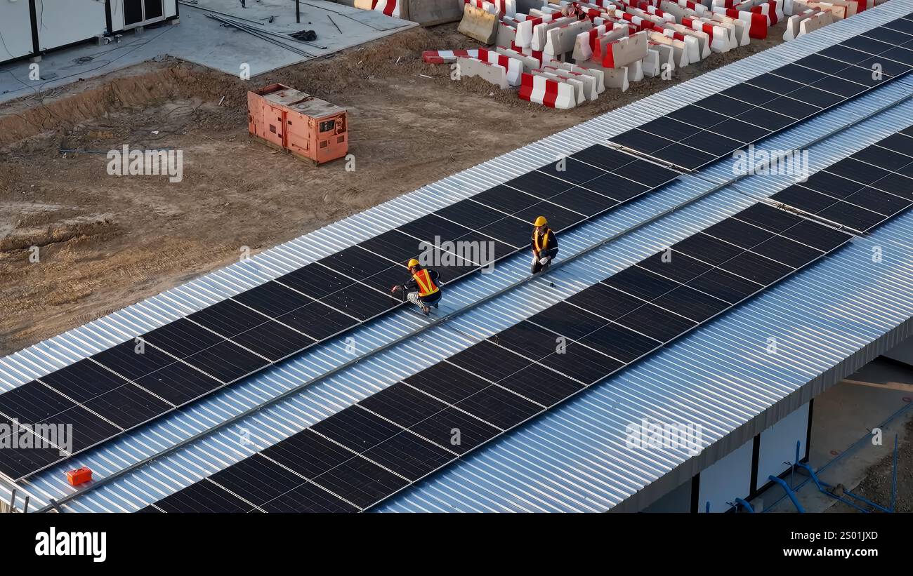 Two workers in safety gear are installing solar panels on a building ...