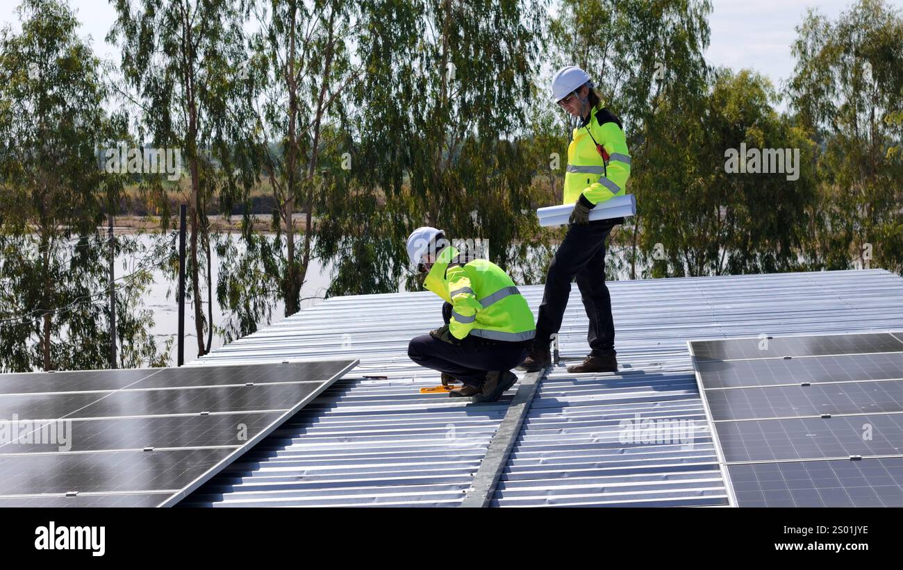 Two workers in safety gear are engaged in the installation of solar ...