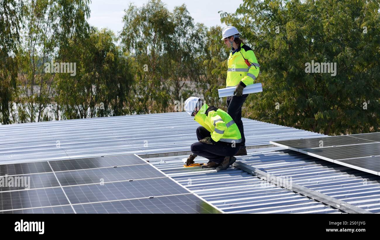 Two construction workers in safety gear install solar panels on a ...