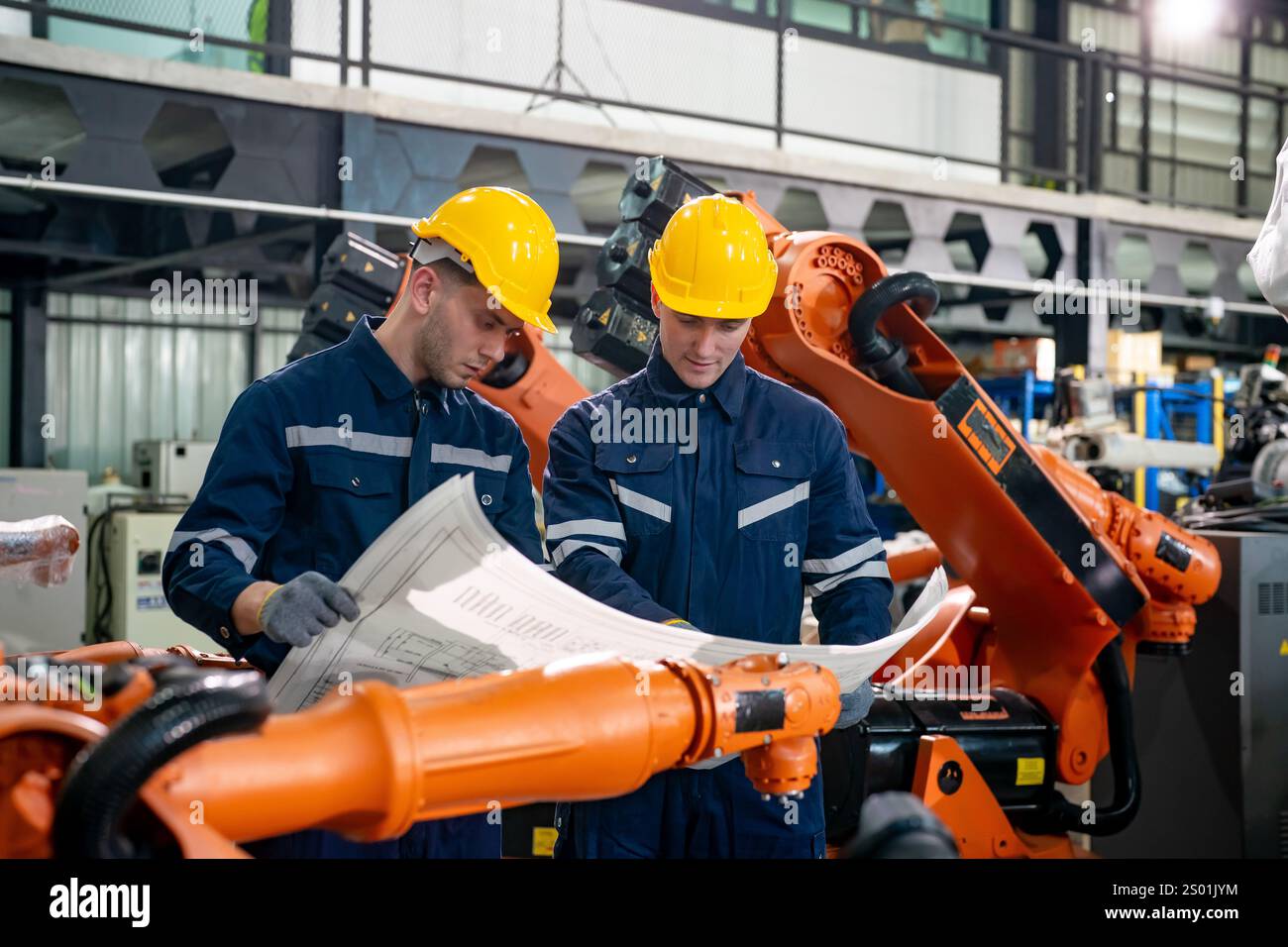 Two engineers wearing safety helmets examine technical plans in a ...