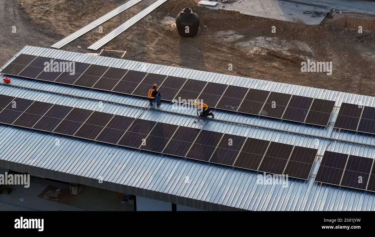 Two workers are installing solar panels on a metal roof at a ...
