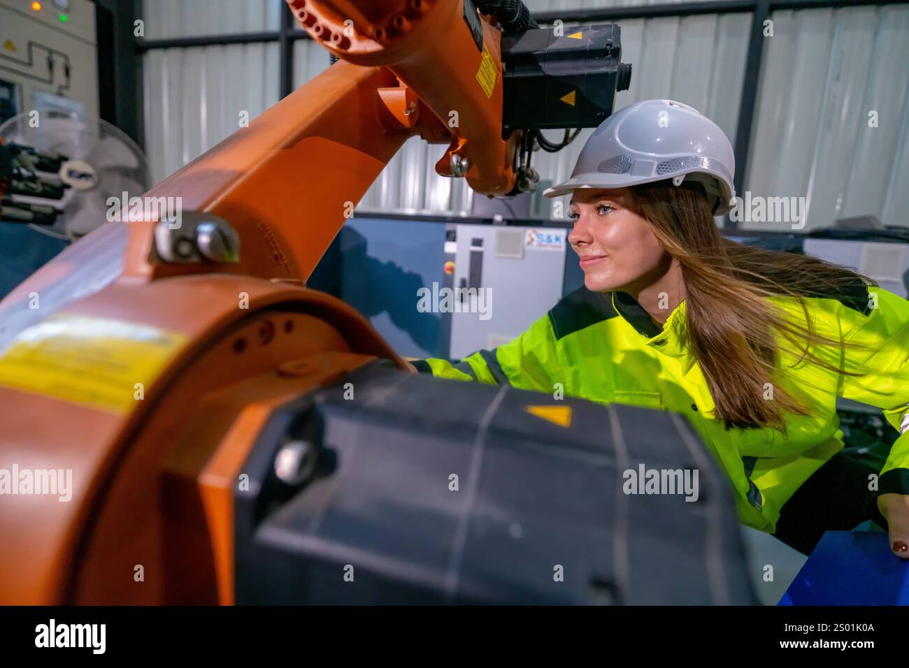 A technician in safety gear examines an industrial robotic arm within a ...