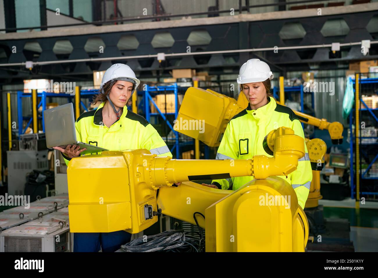 Two engineers in bright yellow jackets and hard hats examine robotic ...
