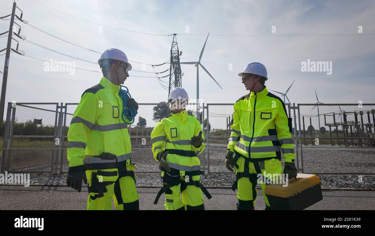 Three workers in bright safety gear are engaged in a discussion near a ...