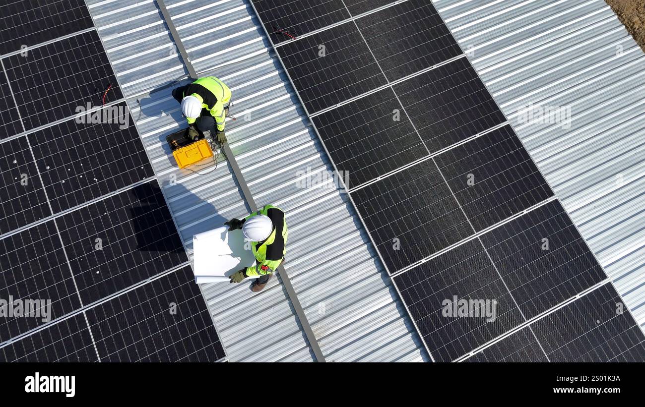 Two workers equipped with safety gear are installing solar panels on a ...