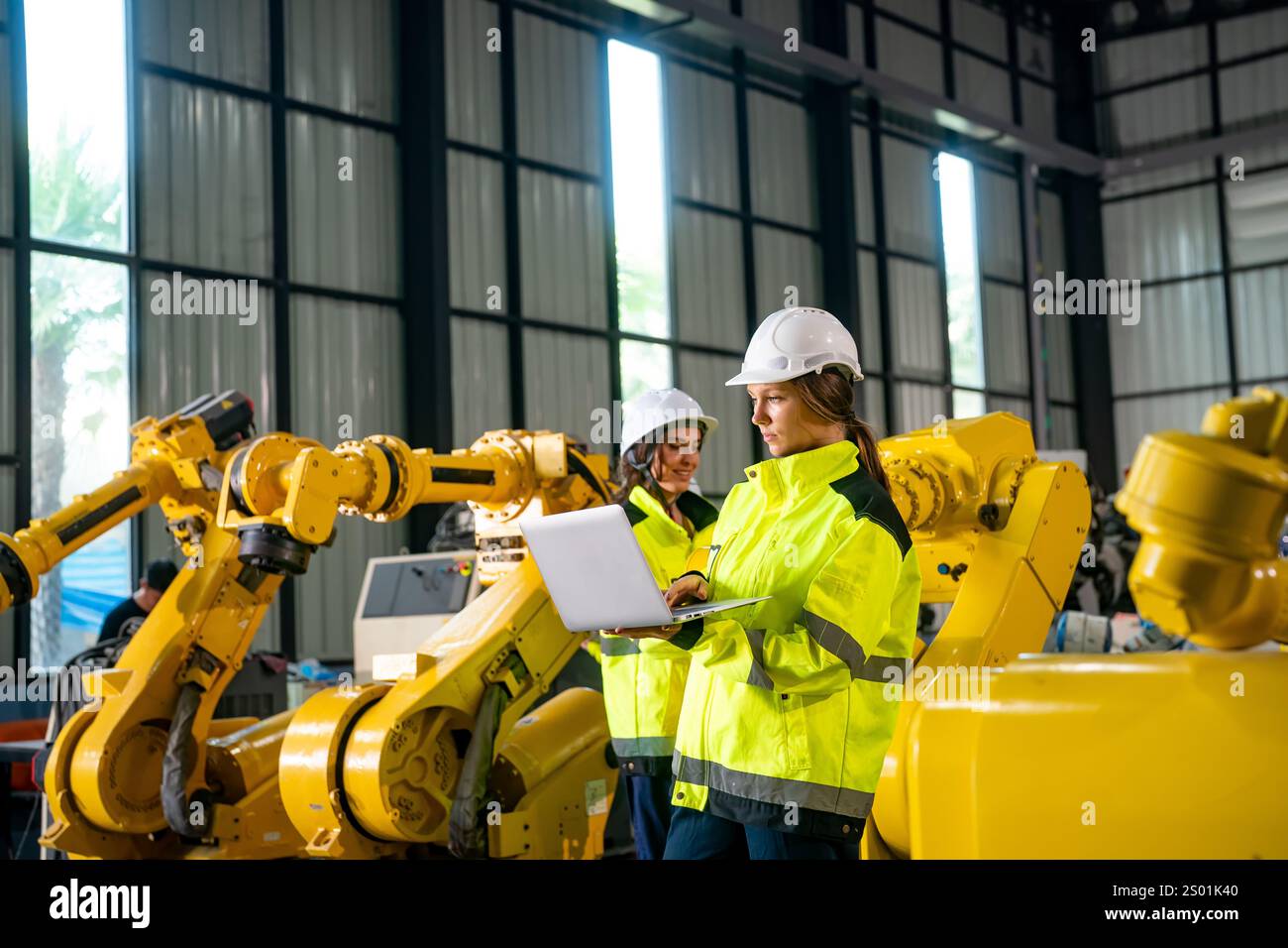 Two engineers in hard hats and safety jackets are operating laptops in ...