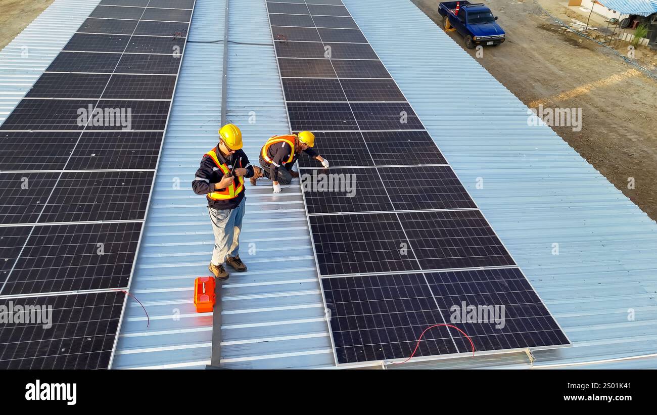 Two workers in safety gear are installing solar panels on a metal ...