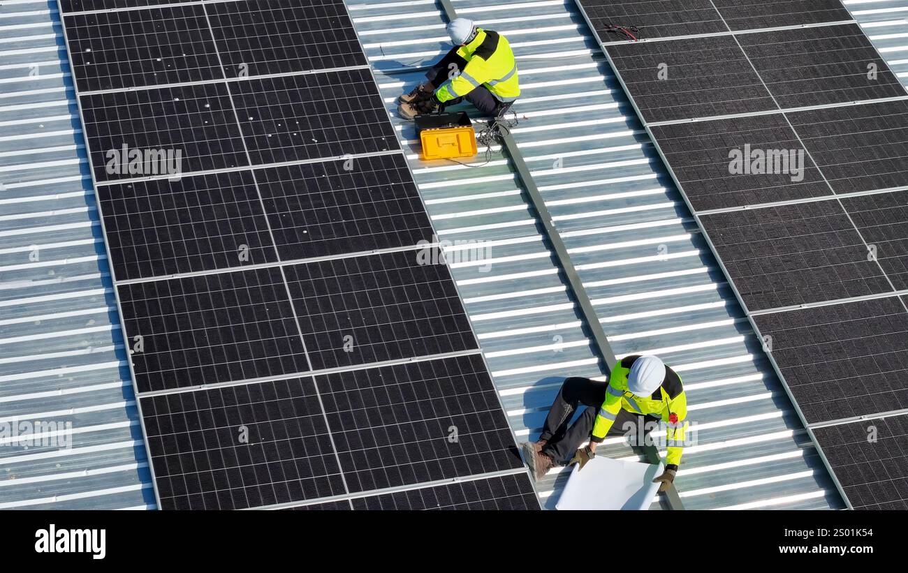 Workers in bright safety vests install solar panels on a metal rooftop ...