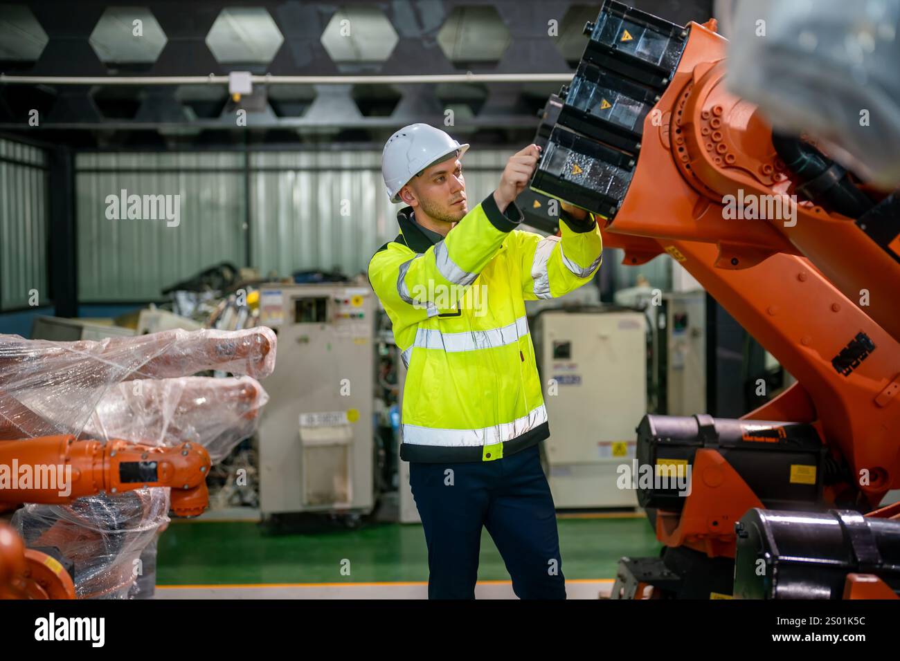 Worker wearing safety gear examines a robotic arm inside a ...