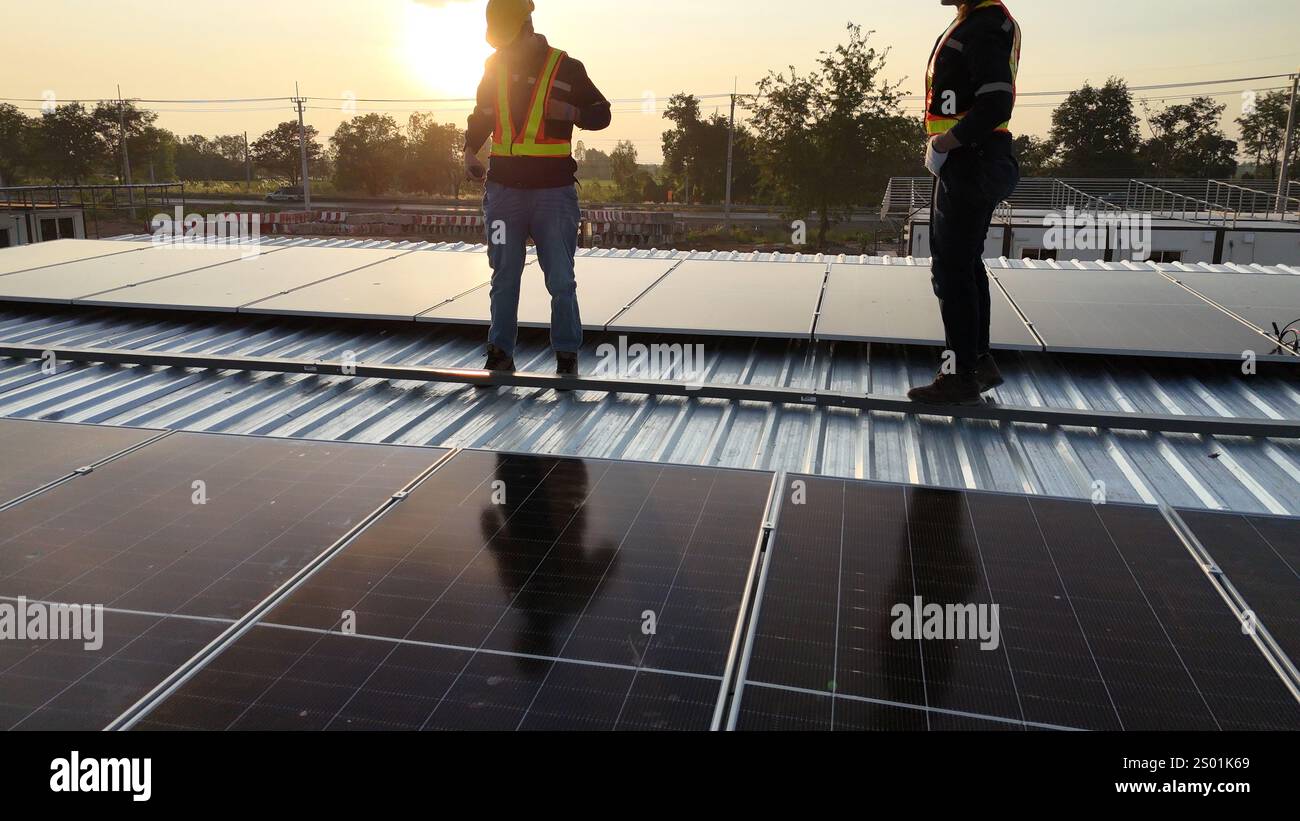 Two workers are positioned on a rooftop, installing solar panels as the sun sets in the ...