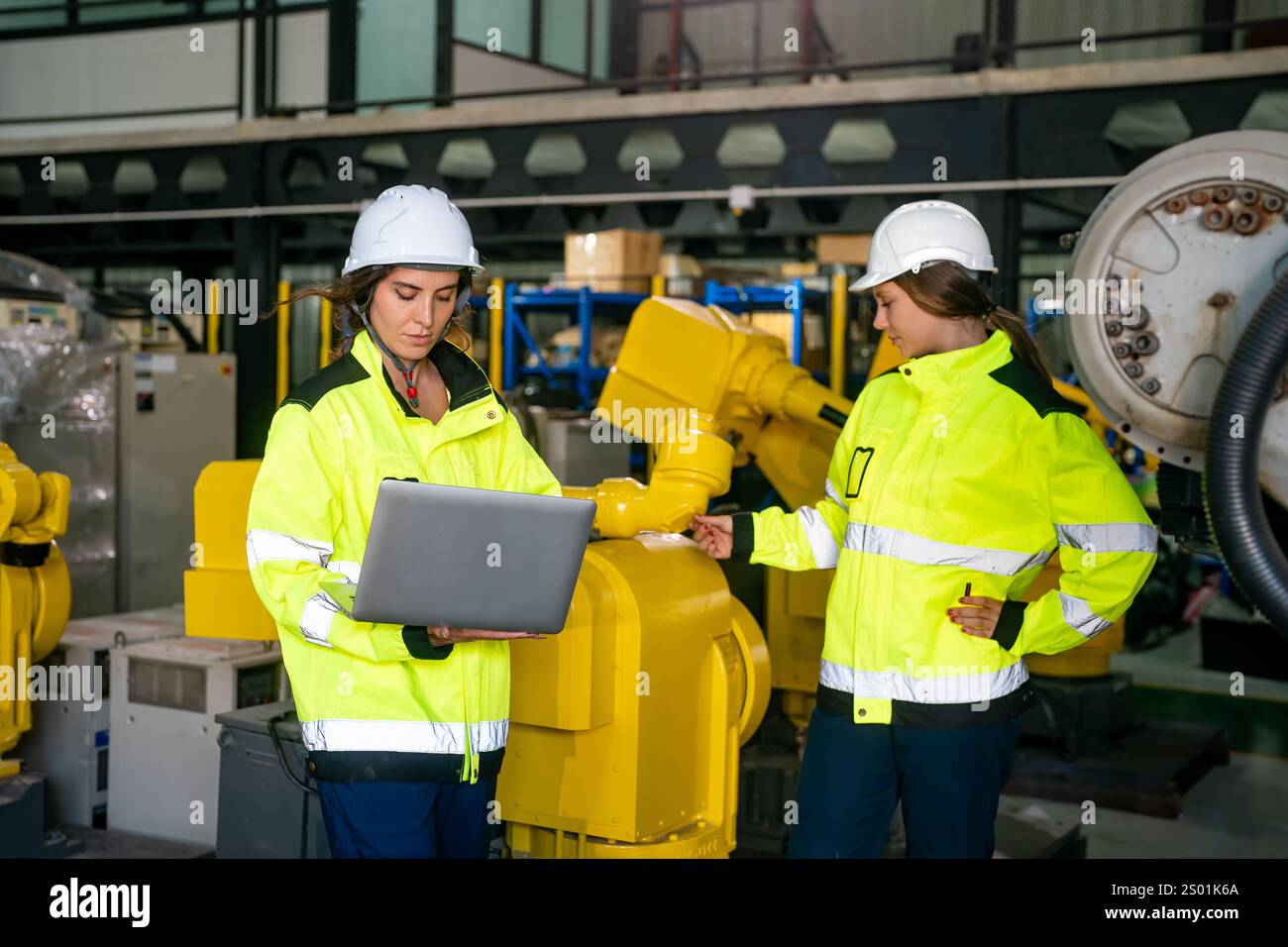 In a busy industrial setting, two women wearing safety gear examine ...