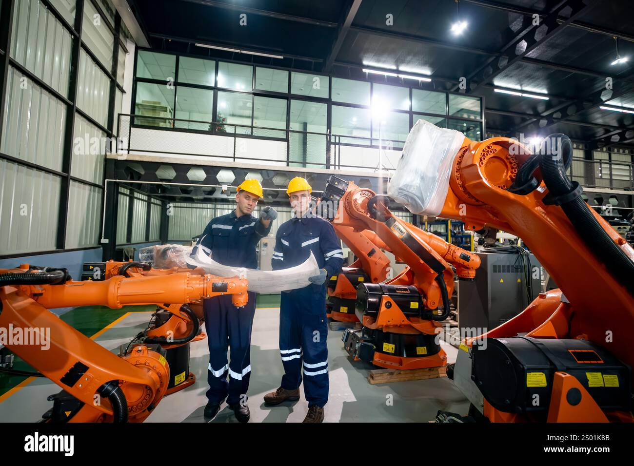 Two technicians in hard hats stand next to robotic arms in a busy ...