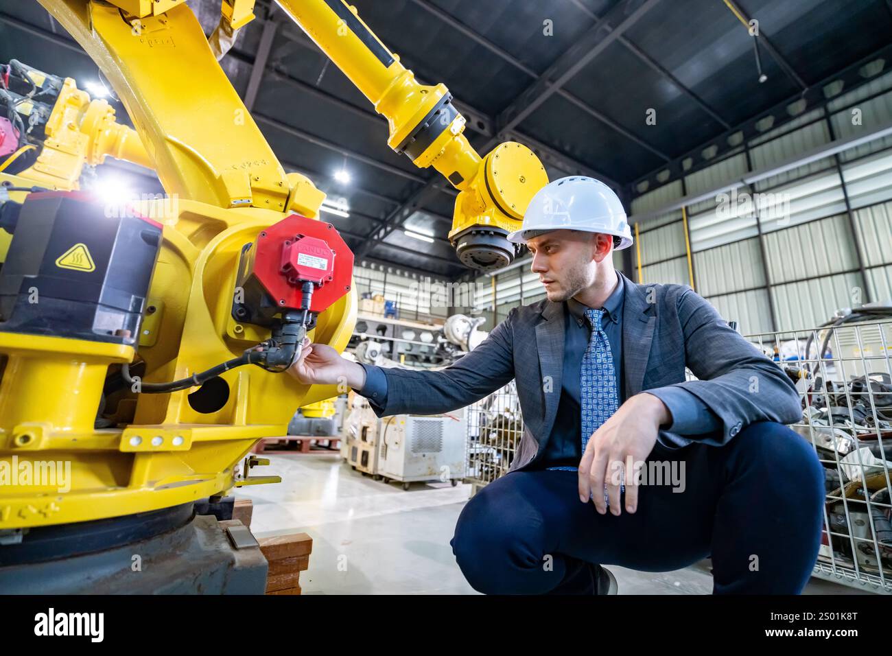 An engineer in formal attire examines a robotic arm in a manufacturing ...