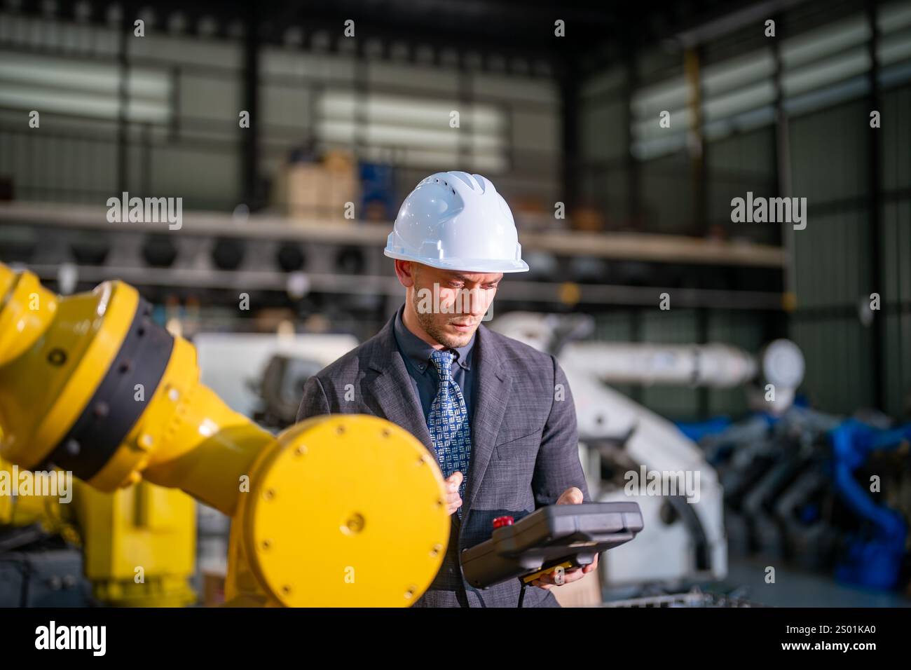 A worker in a hard hat examines equipment while using a handheld device ...