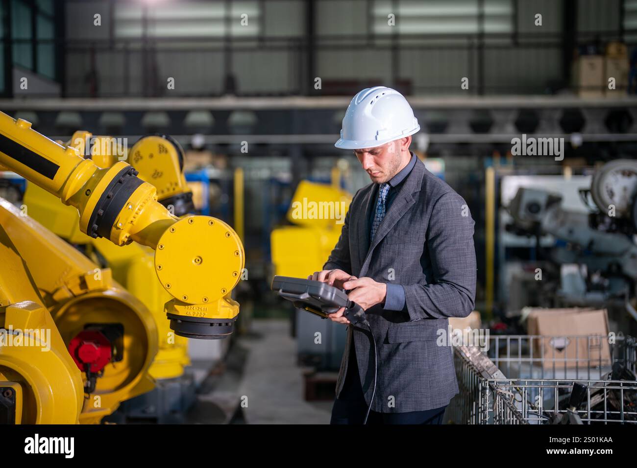 A professional in a suit inspects robotic arms in a busy manufacturing ...