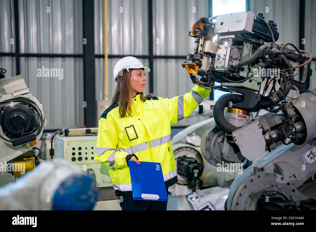 A professional wearing a hard hat and high-visibility jacket closely examines robotic equipment ...