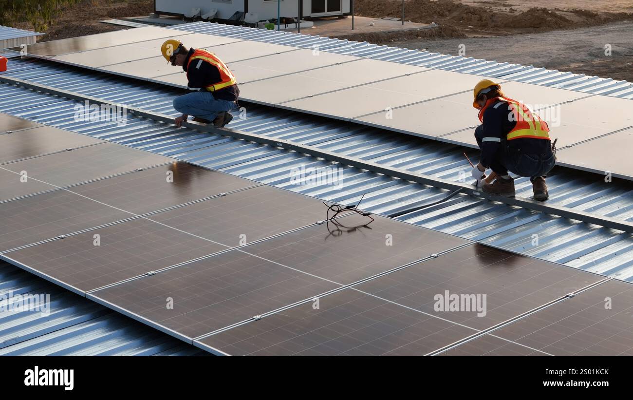 Two workers wearing safety helmets and vests secure solar panels on a ...