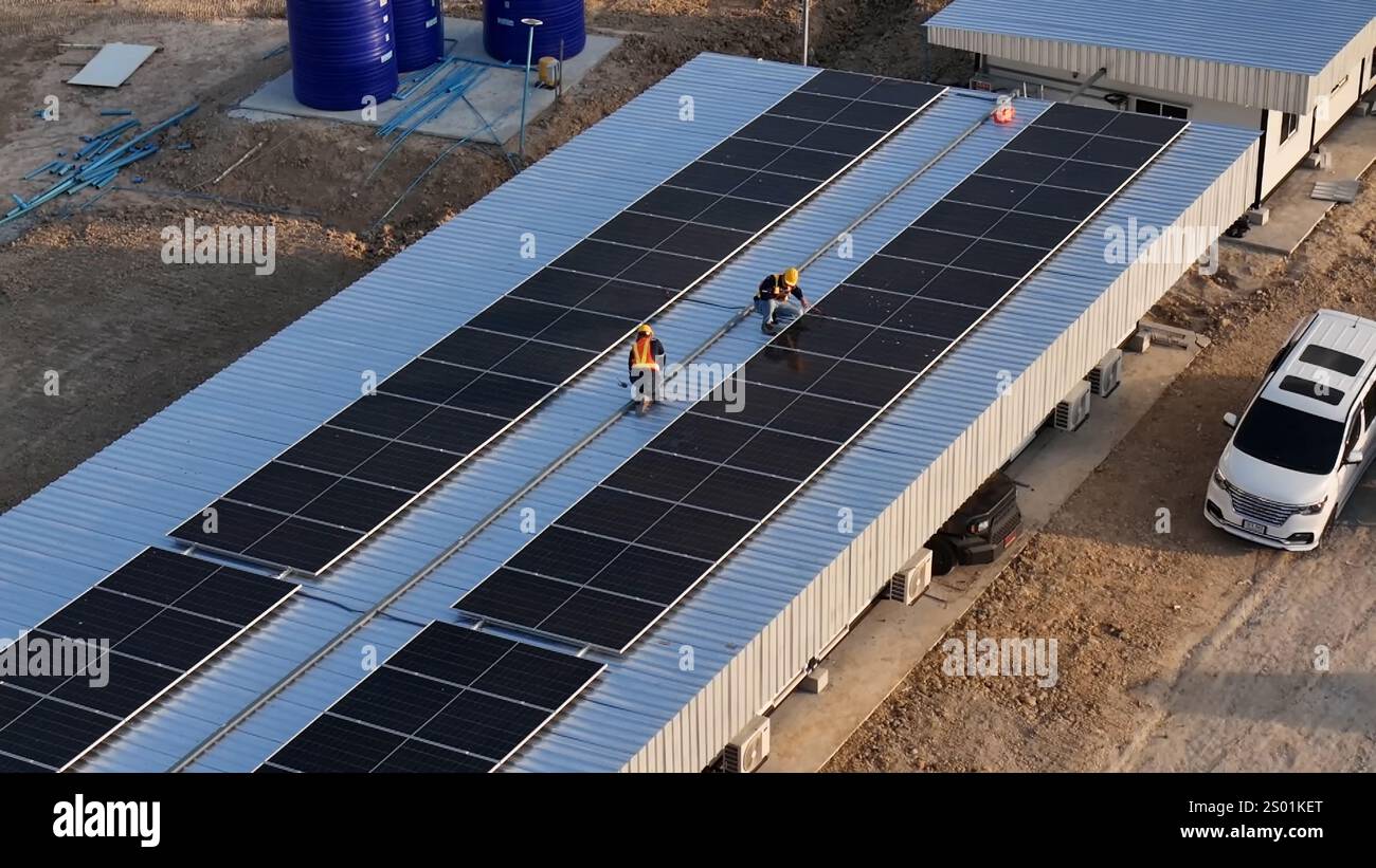 Workers install solar panels on the roof of a recently built structure ...