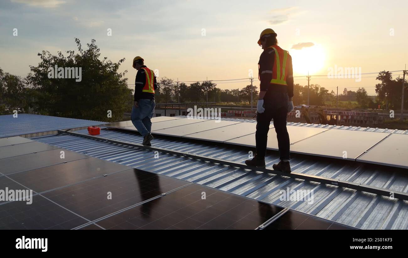 Two workers wearing safety gear install solar panels on a rooftop ...