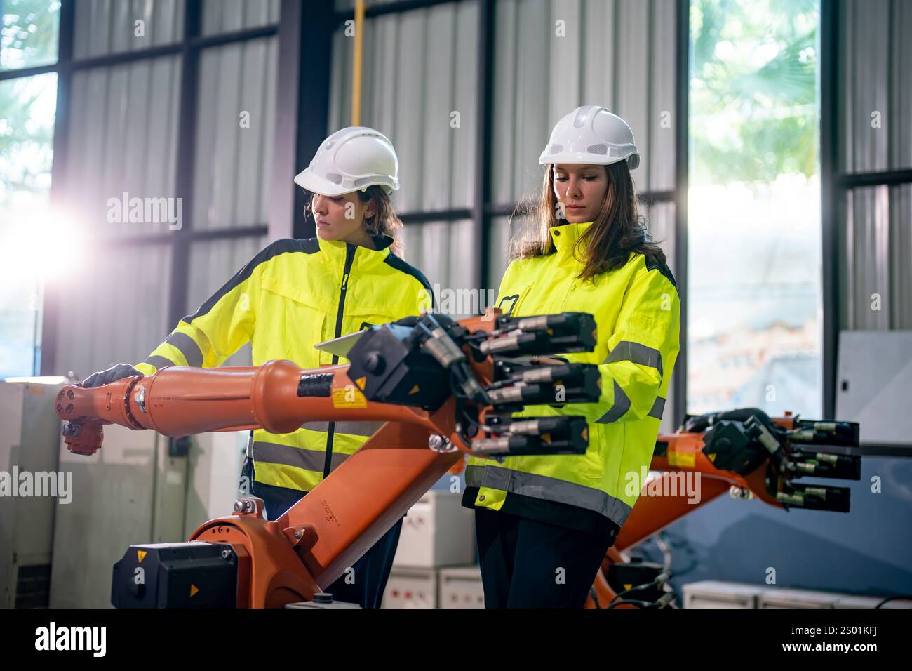 Two individuals in safety gear are focused on controlling a robotic arm ...
