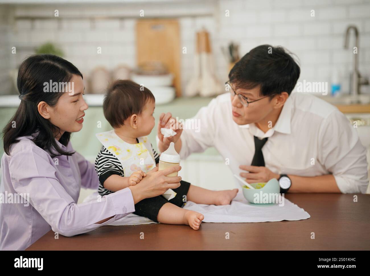 A mother assists her partner in feeding their baby, creating a warm and ...