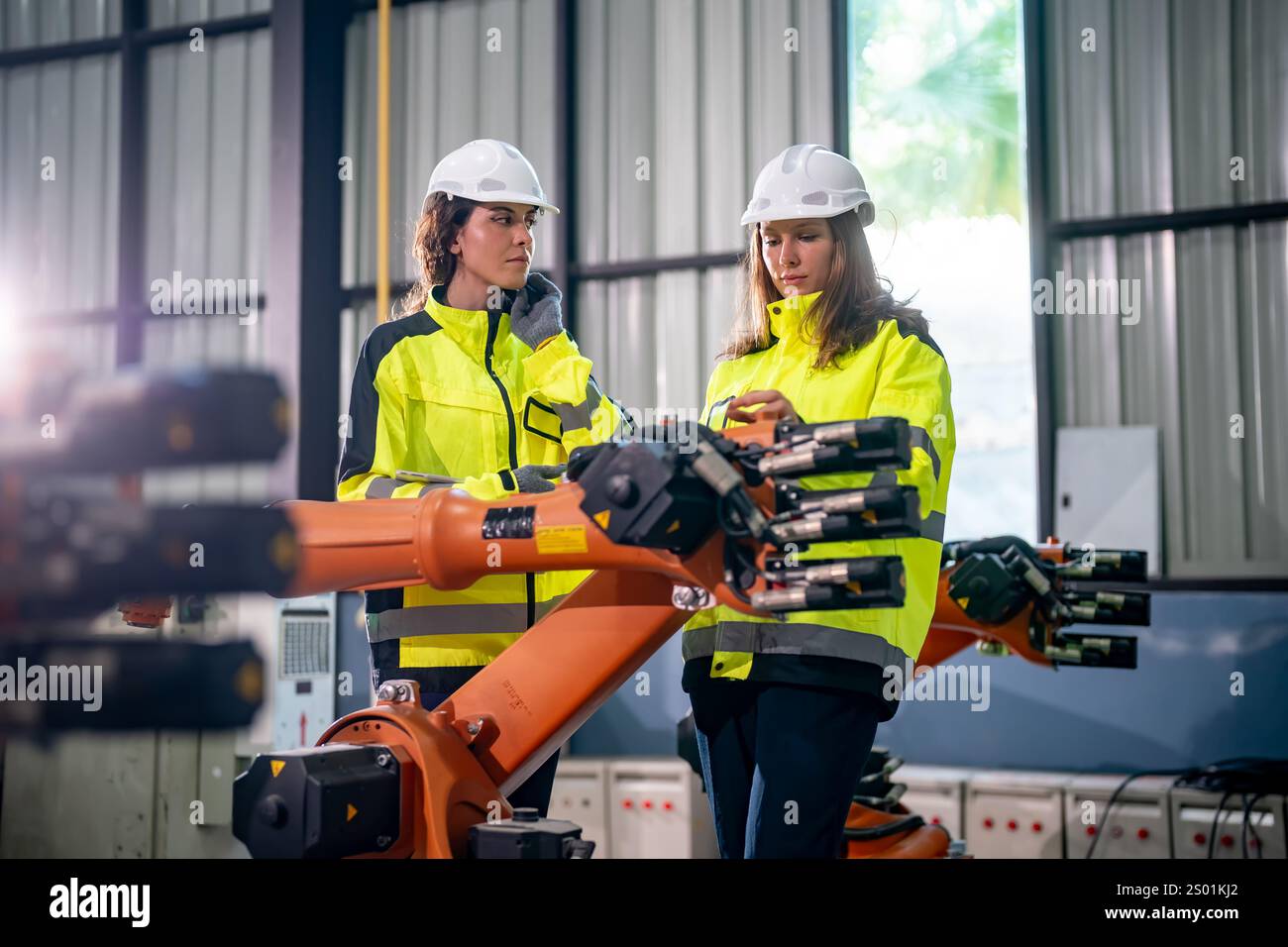 Two female engineers in bright safety gear discuss a robotics project ...
