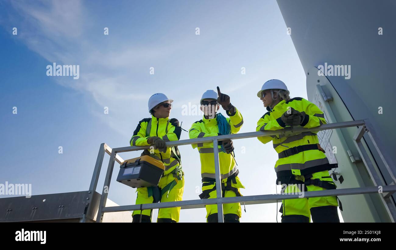 Three workers in bright yellow safety gear gather on a platform at a ...