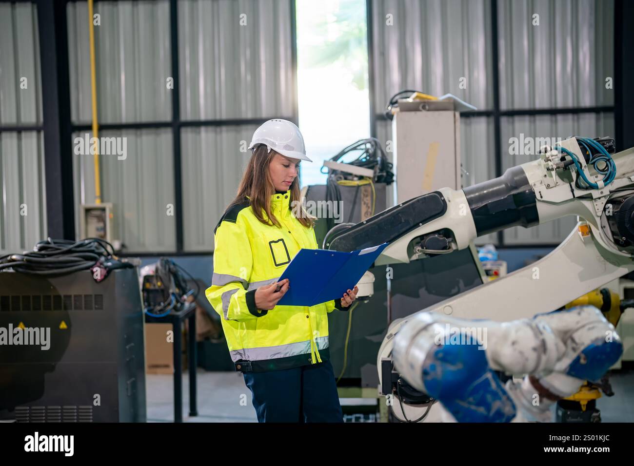 A young engineer in a high-visibility jacket and hard hat reviews an ...
