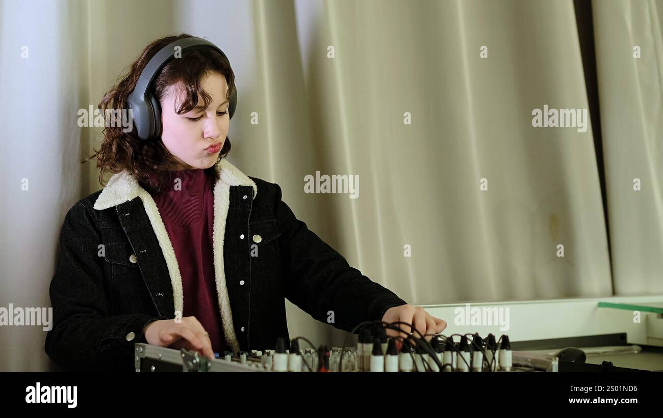 A girl with headphones enjoys working on a sound mixer, her expression ...