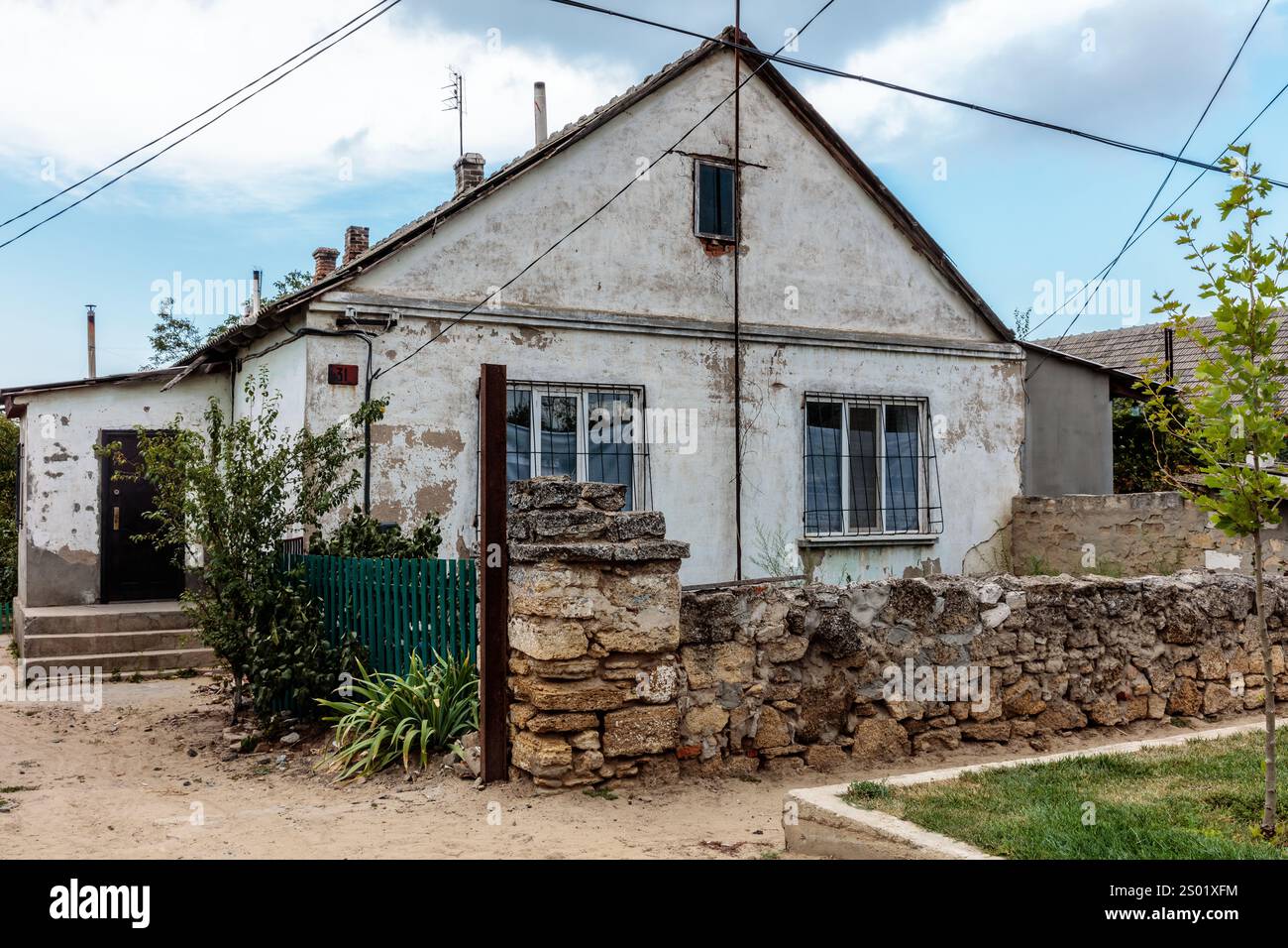 A small house with a stone wall and a green fence. The house is old and ...