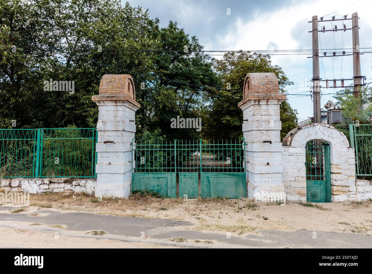 A green gate with a white archway sits in front of a large stone wall ...