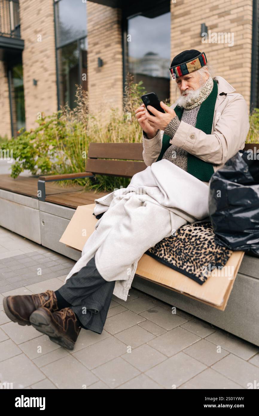 Vertical portrait of older man sitting on city bench, using typing ...