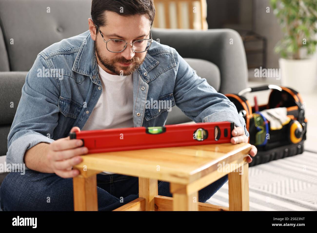Man using level tool while repairing wooden stool at home Stock Photo ...