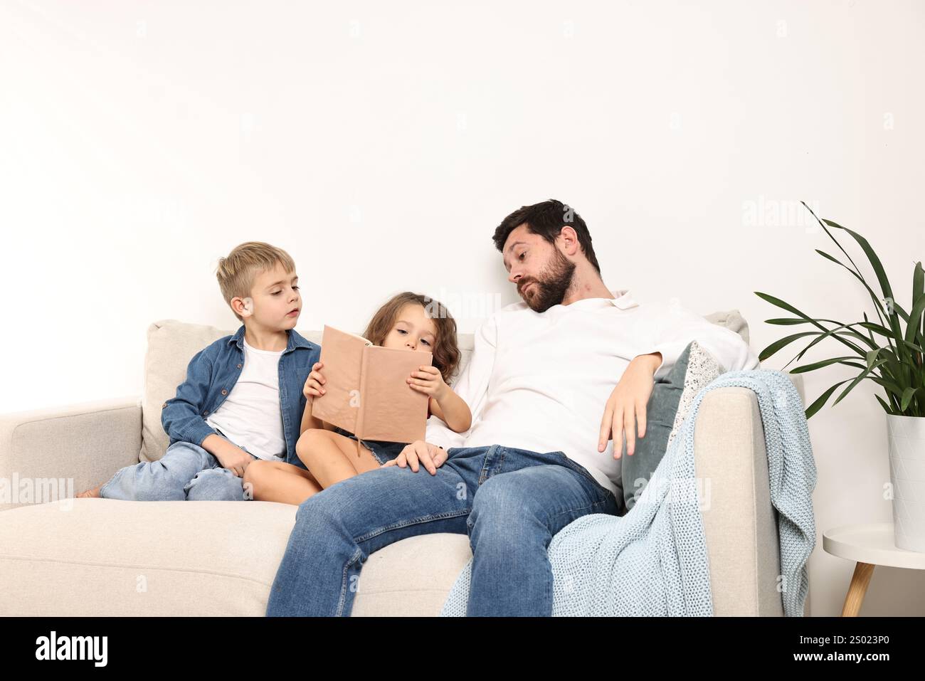 Overwhelmed father and his children reading book on sofa at home Stock ...