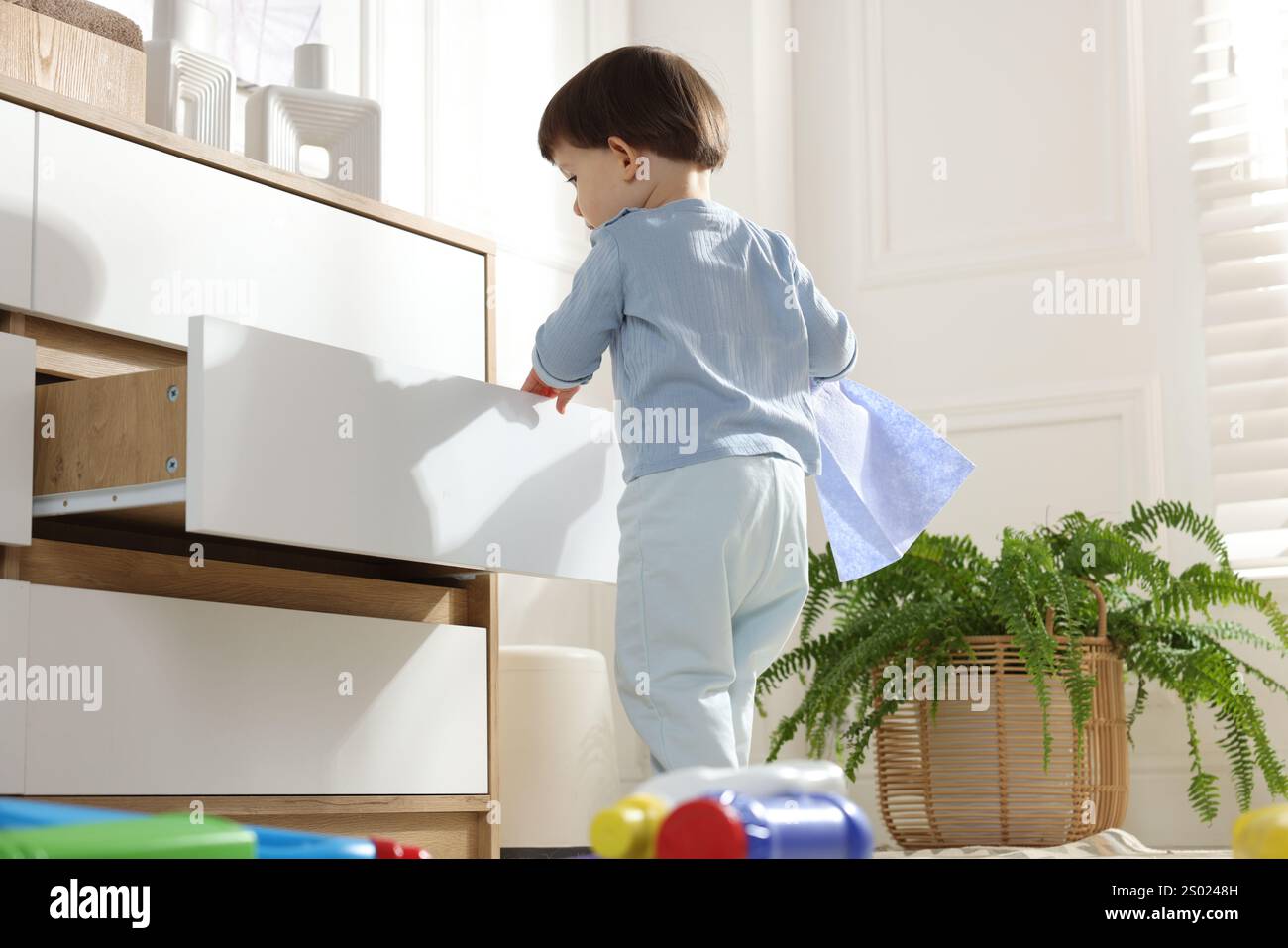 Little boy opening drawer with bottles of detergents at home, back view ...
