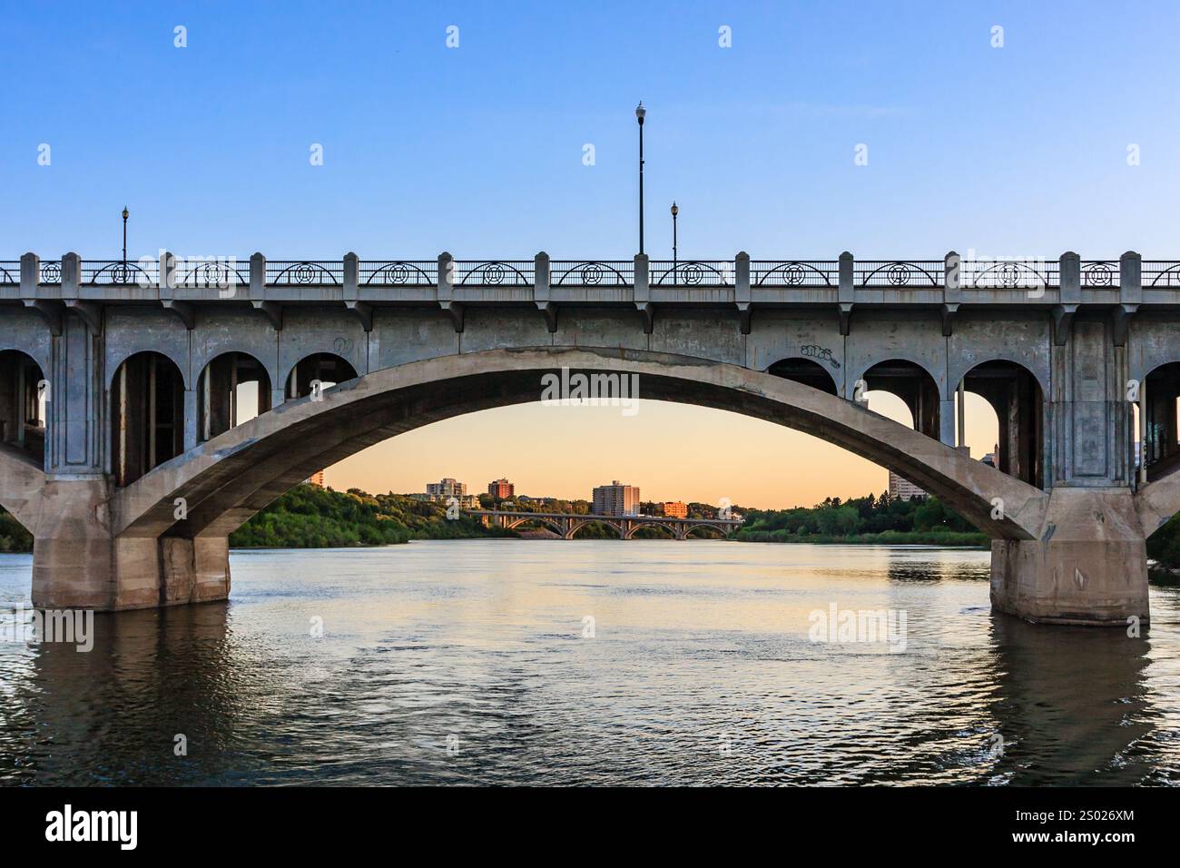 A bridge spans a river with a city in the background. The bridge is ...