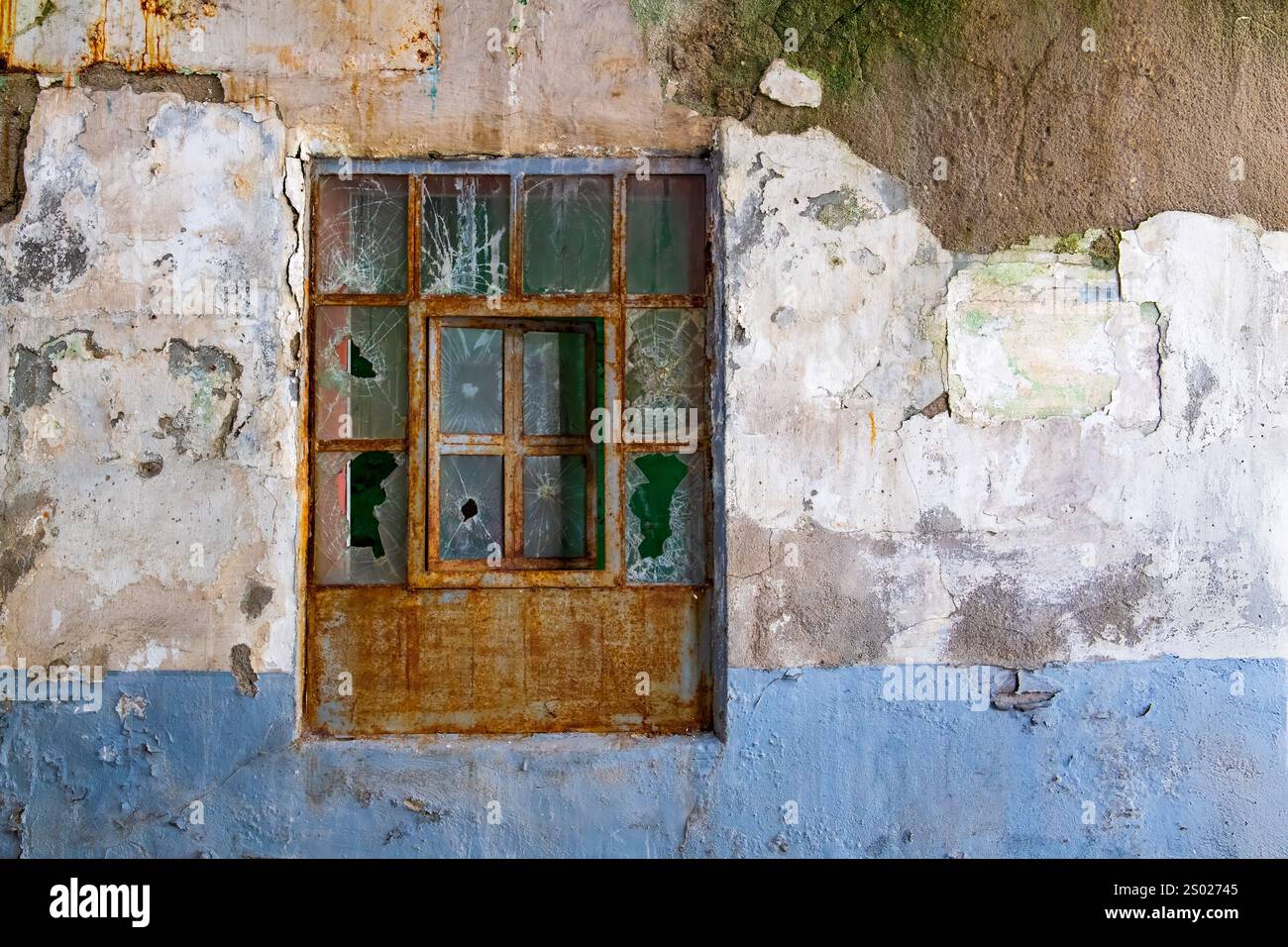 A rusted window with broken glass set in a cracked, weathered wall with ...