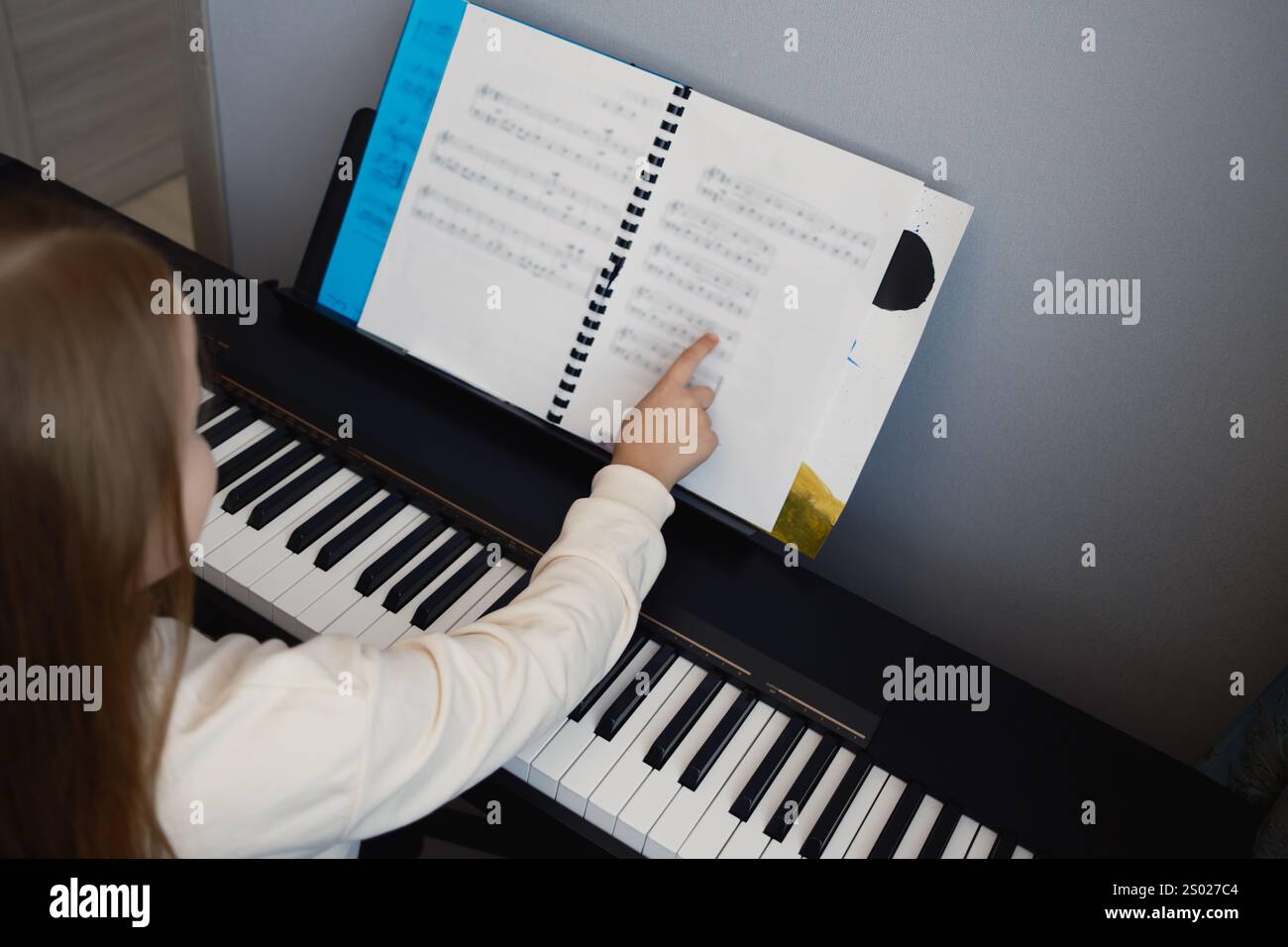 Young girl learning to play piano while reading music from a sheet ...
