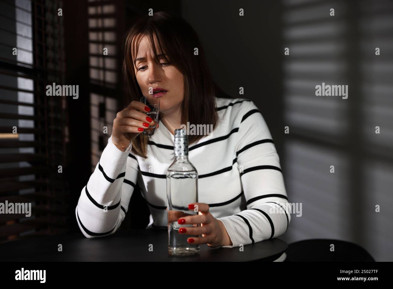 Alcohol addiction. Woman with shot glass of vodka and bottle at table ...