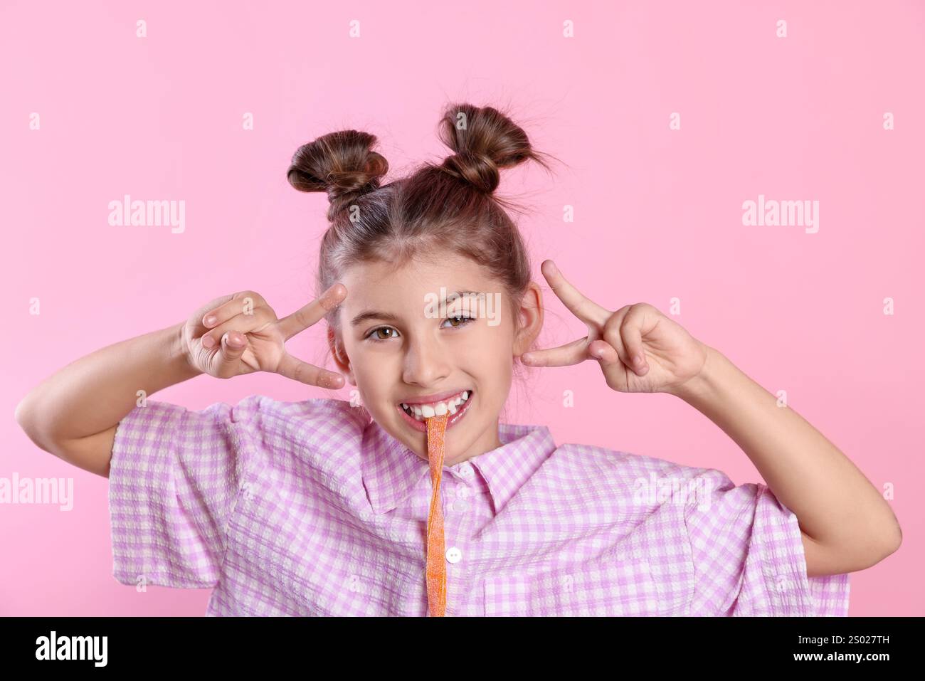 Happy girl eating tasty gummy candy and showing peace signs on pink ...