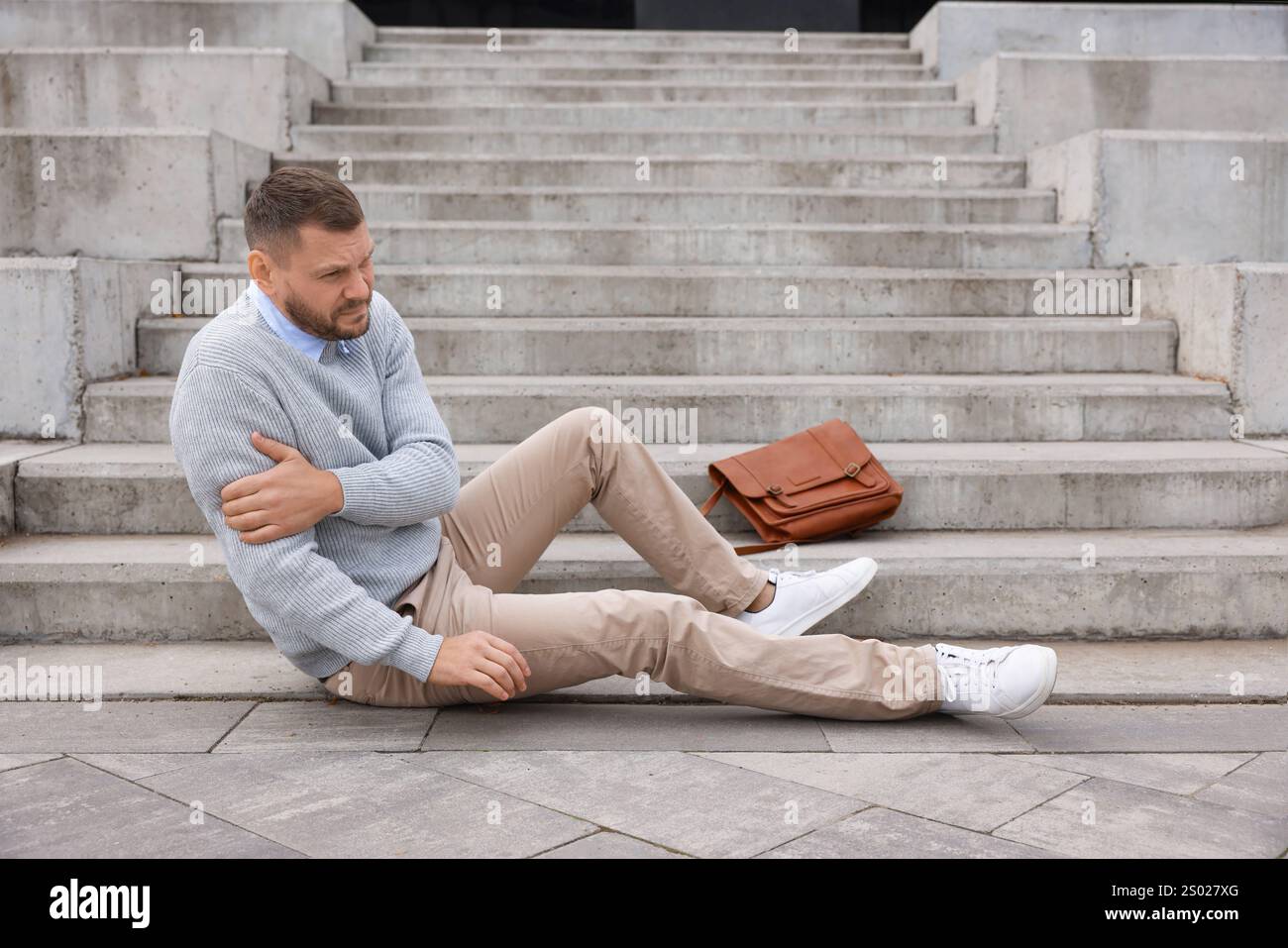 Man with injured arm on stairs outdoors after fall. Dangerous accident ...