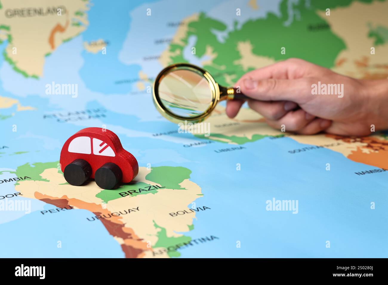 Woman looking at world map through magnifying glass, focus on red toy ...