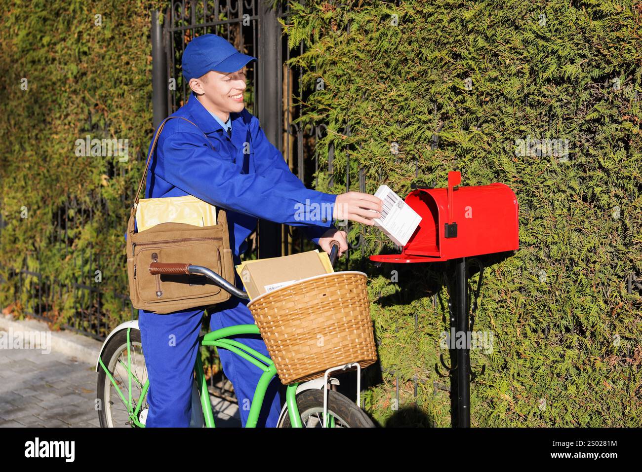 Postman with bicycle putting parcel into mail box outdoors Stock Photo ...