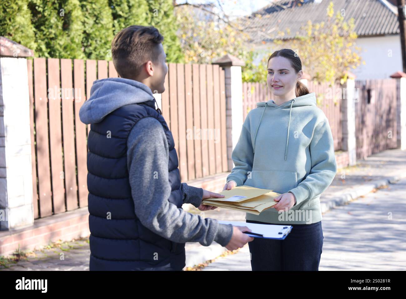 Postman with clipboard giving envelopes to woman outdoors Stock Photo ...