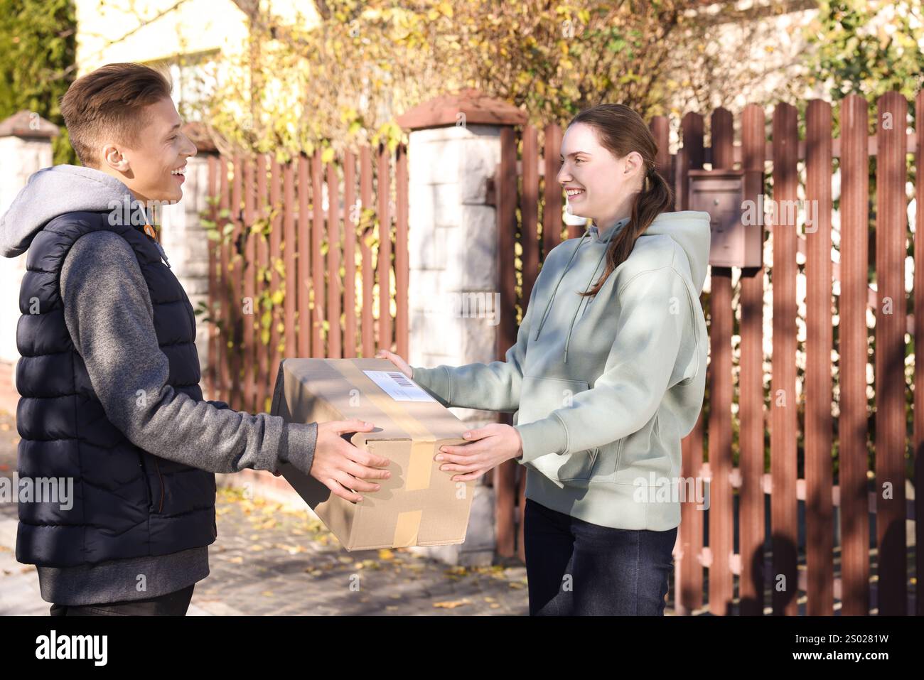 Postman giving parcel box to woman outdoors Stock Photo - Alamy