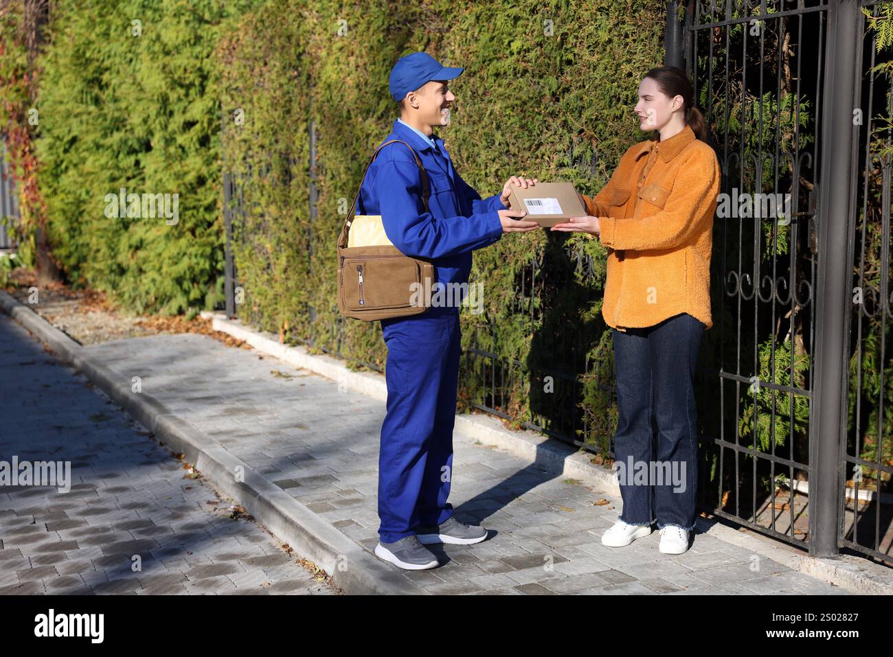 Woman receiving parcel from postman outdoors. Mail service Stock Photo ...