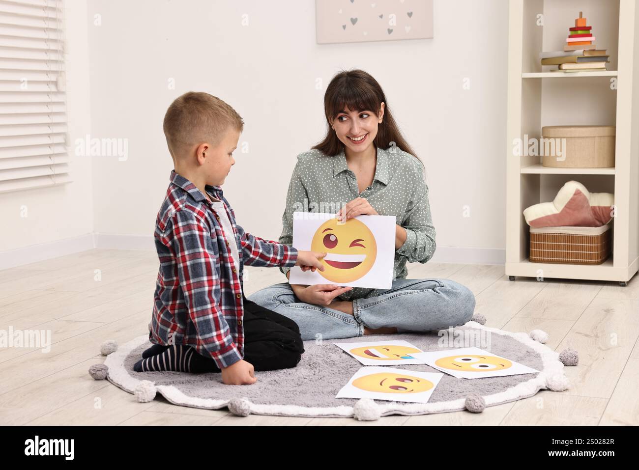 Autism therapy. Little boy choosing emoticon with smiling psychologist ...